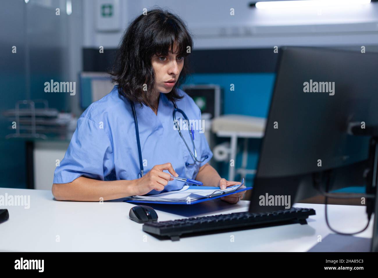 Medical assistant analyzing documents and files on monitor at night ...