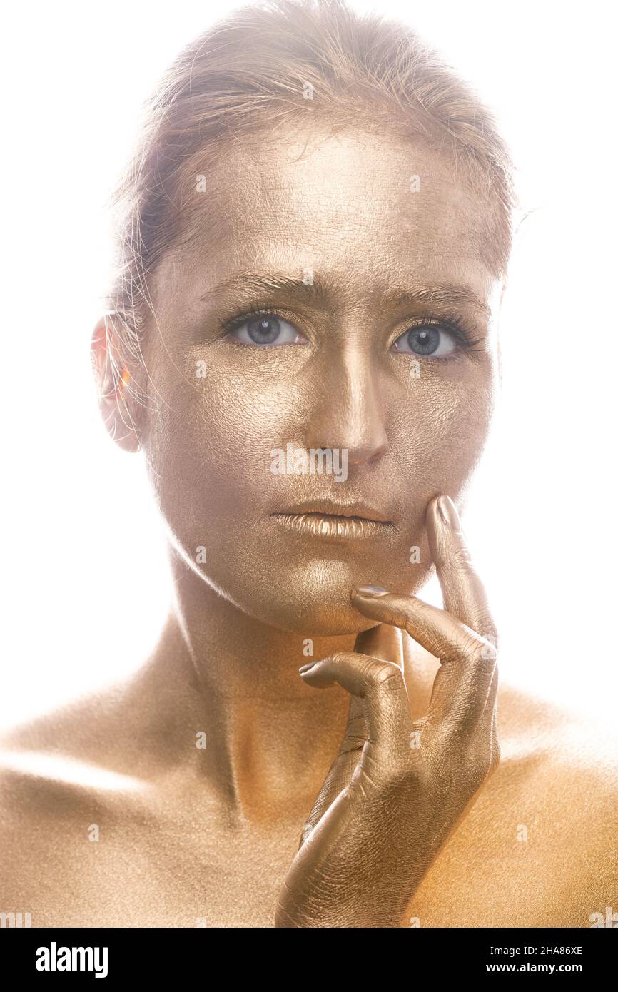 Beautiful woman painted gold looking to camera with her fingers lightly ...