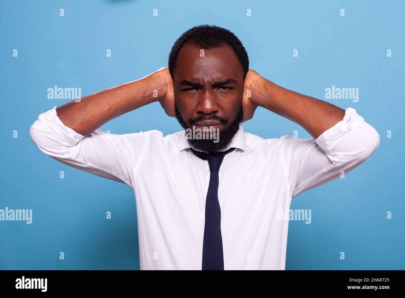 Portrait of standing frowning businessman covering ears to stop hearing ...