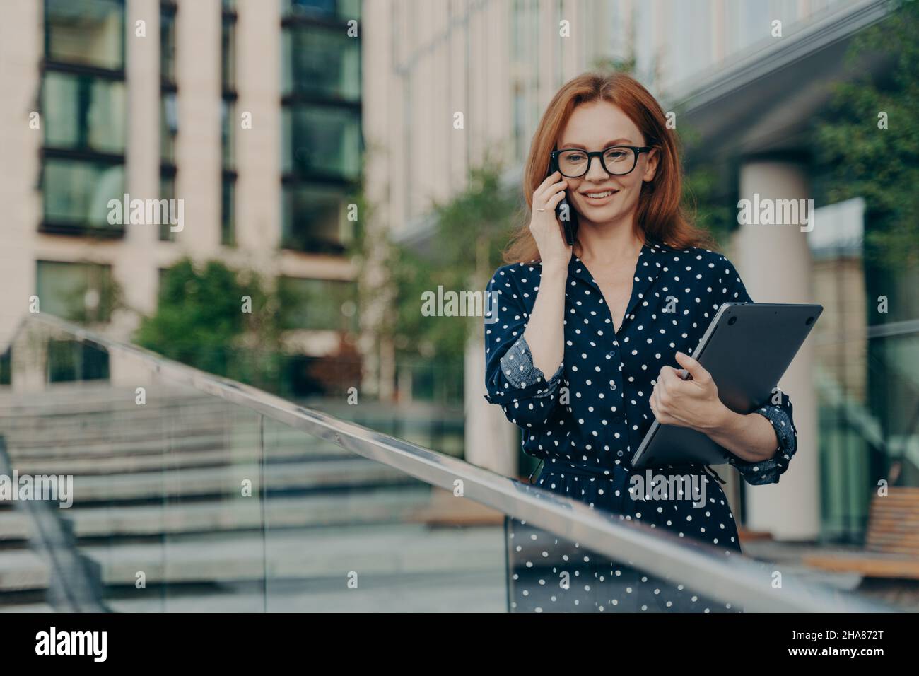 Redhead woman in trendy clothes has telephone conversation walks on ...