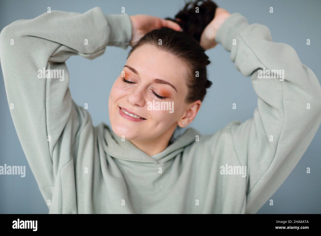 Satisfied delighted woman with glitter makeup, wears casual cozy ...