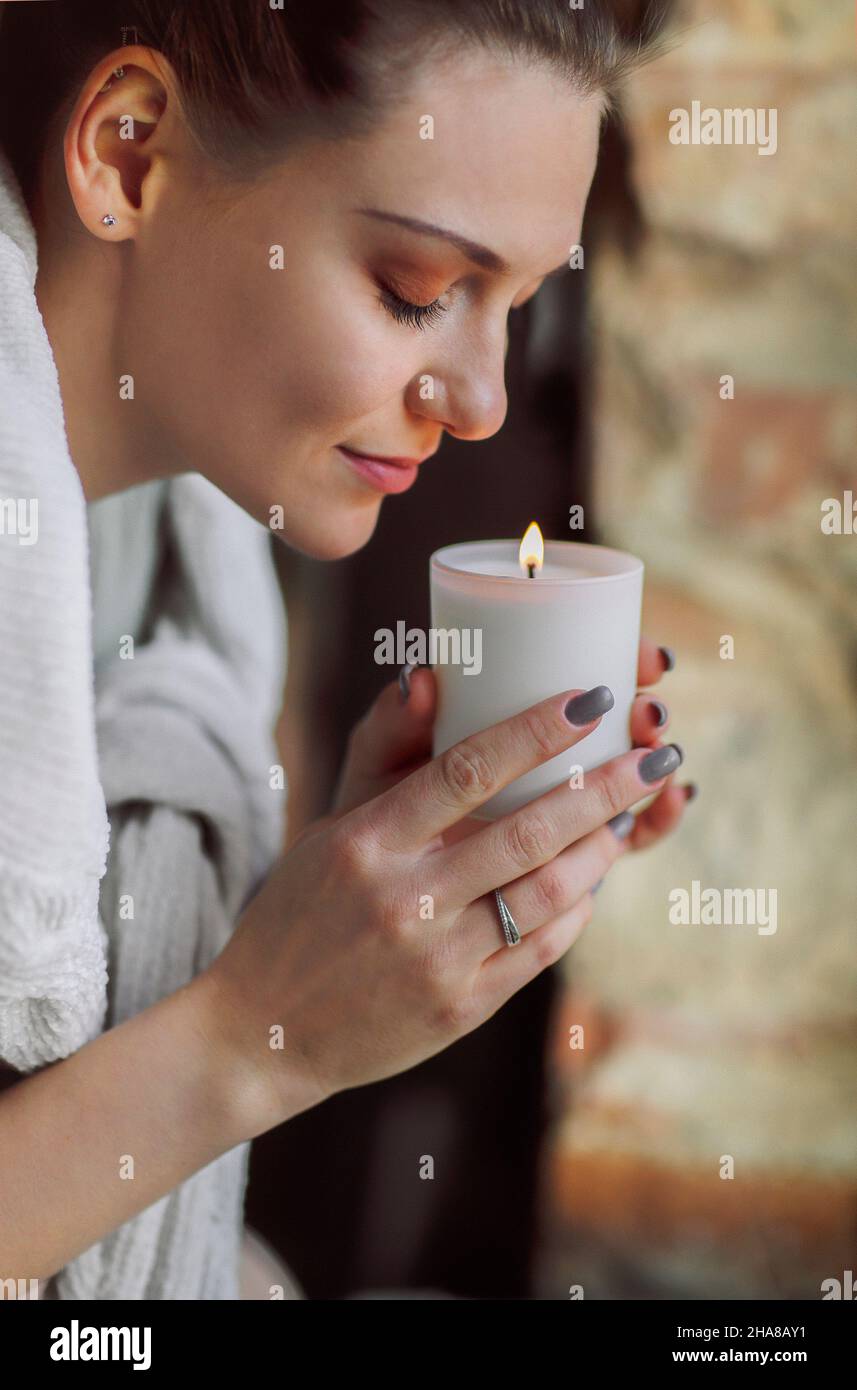 Side portrait of young calm woman holding lit candle in hands, closing ...