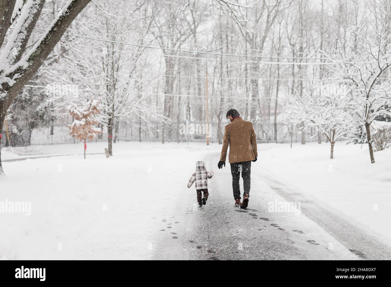 Dad and toddler walk down street on a snowy day in a neighborhood Stock ...