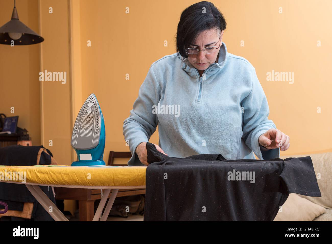 Middle-aged woman in cyan tracksuit ironing a black T-shirt on an ...