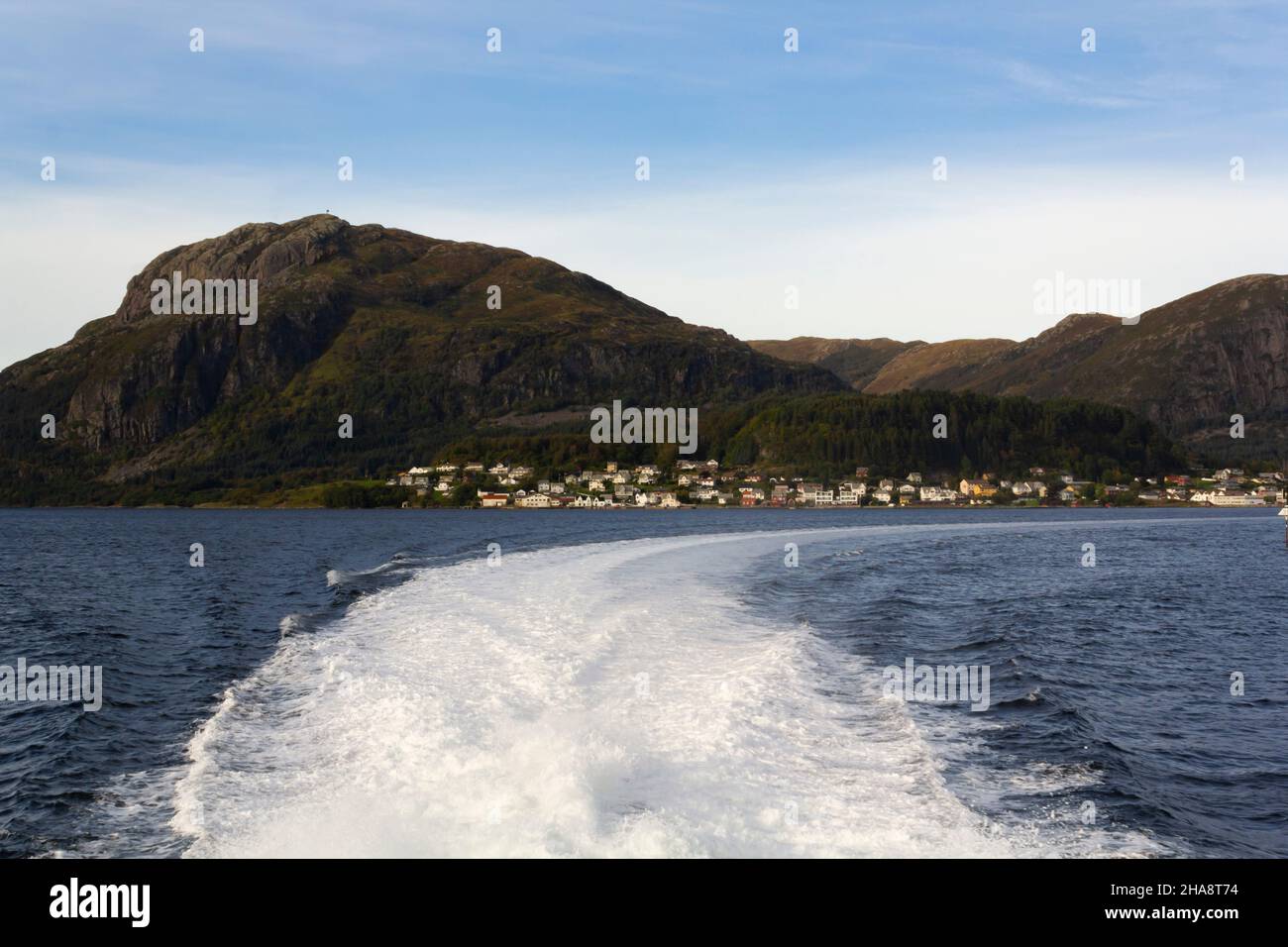 Trail on water of fast moving boat with mountains and houses on the ...