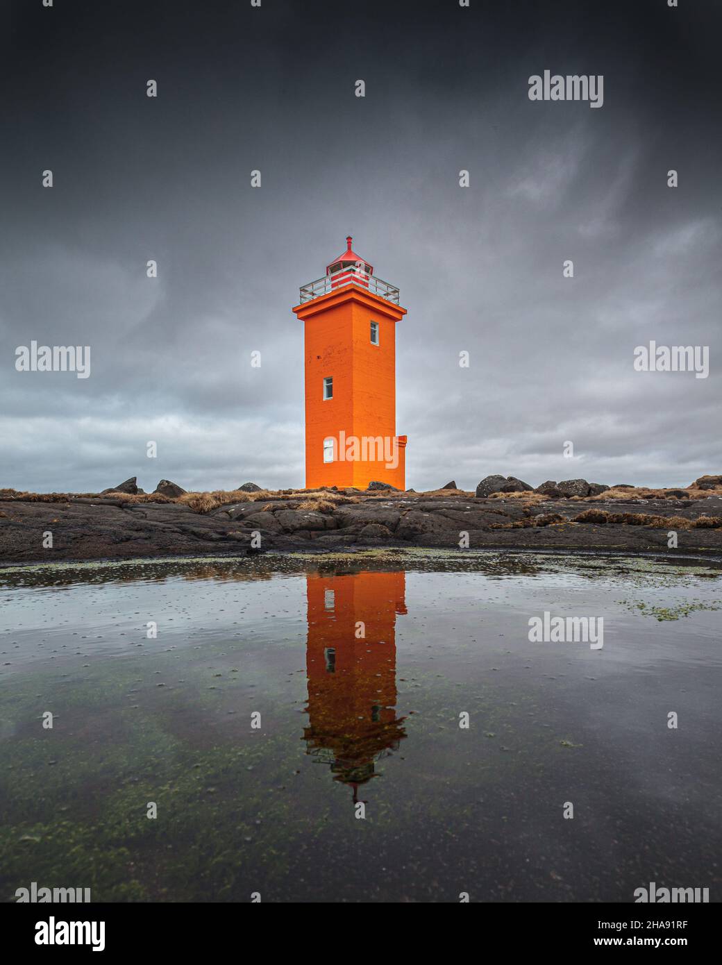 Beautiful view of an orange lighthouse and its reflection in the water ...