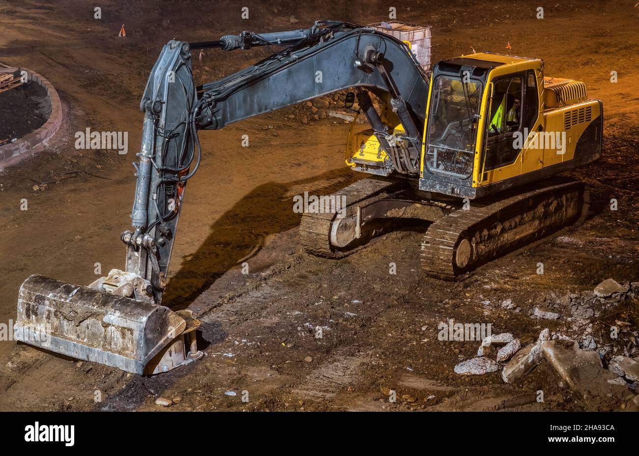 A yellow digger excavator parked during the night on a construction ...