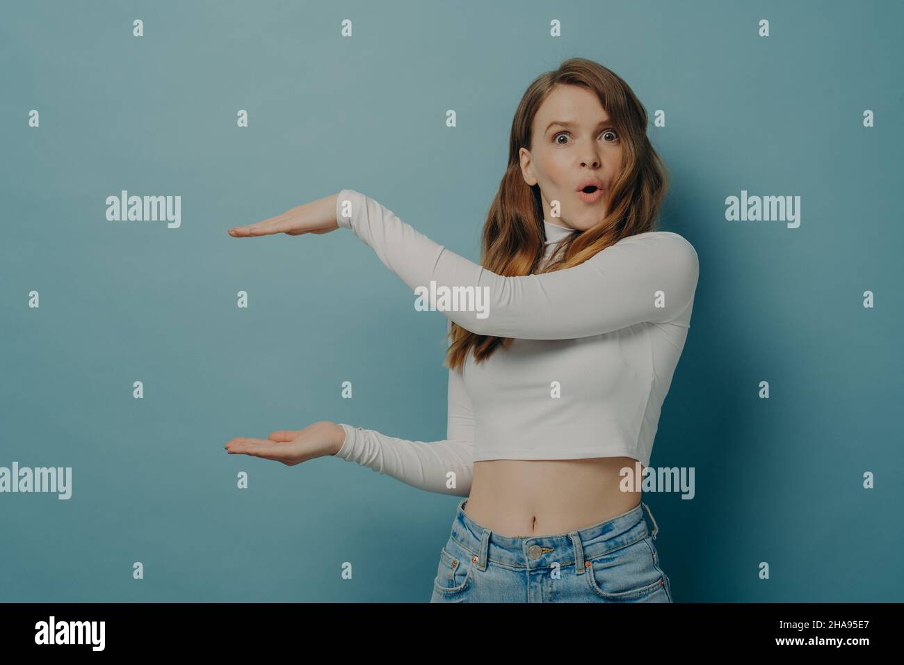 Surprised amazed young woman shows something big in size with hands ...