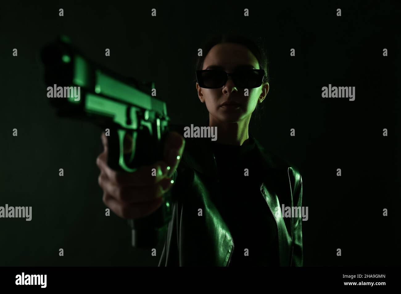 Woman with gun dressed in matrix style on dark background Stock Photo ...