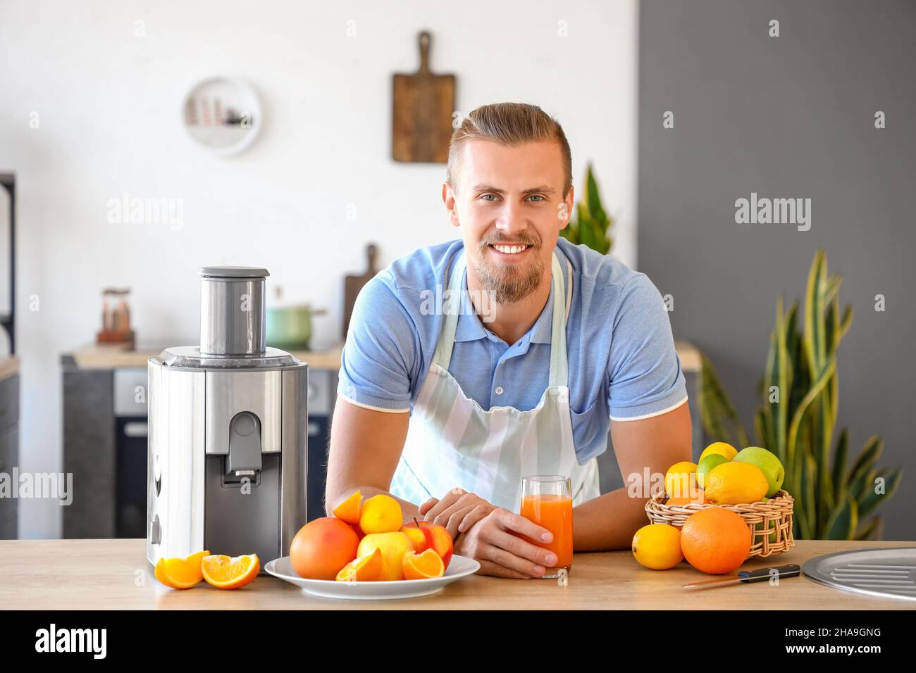 Young man with glass of fresh fruit juice near modern juicer in kitchen ...