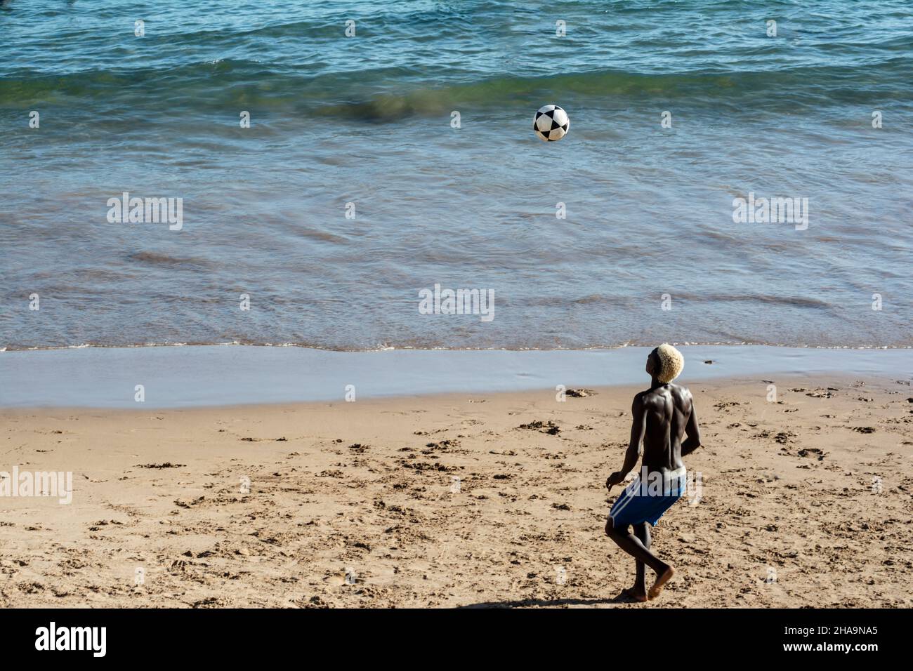 Young model playing sand football on the beach under strong summer sun ...