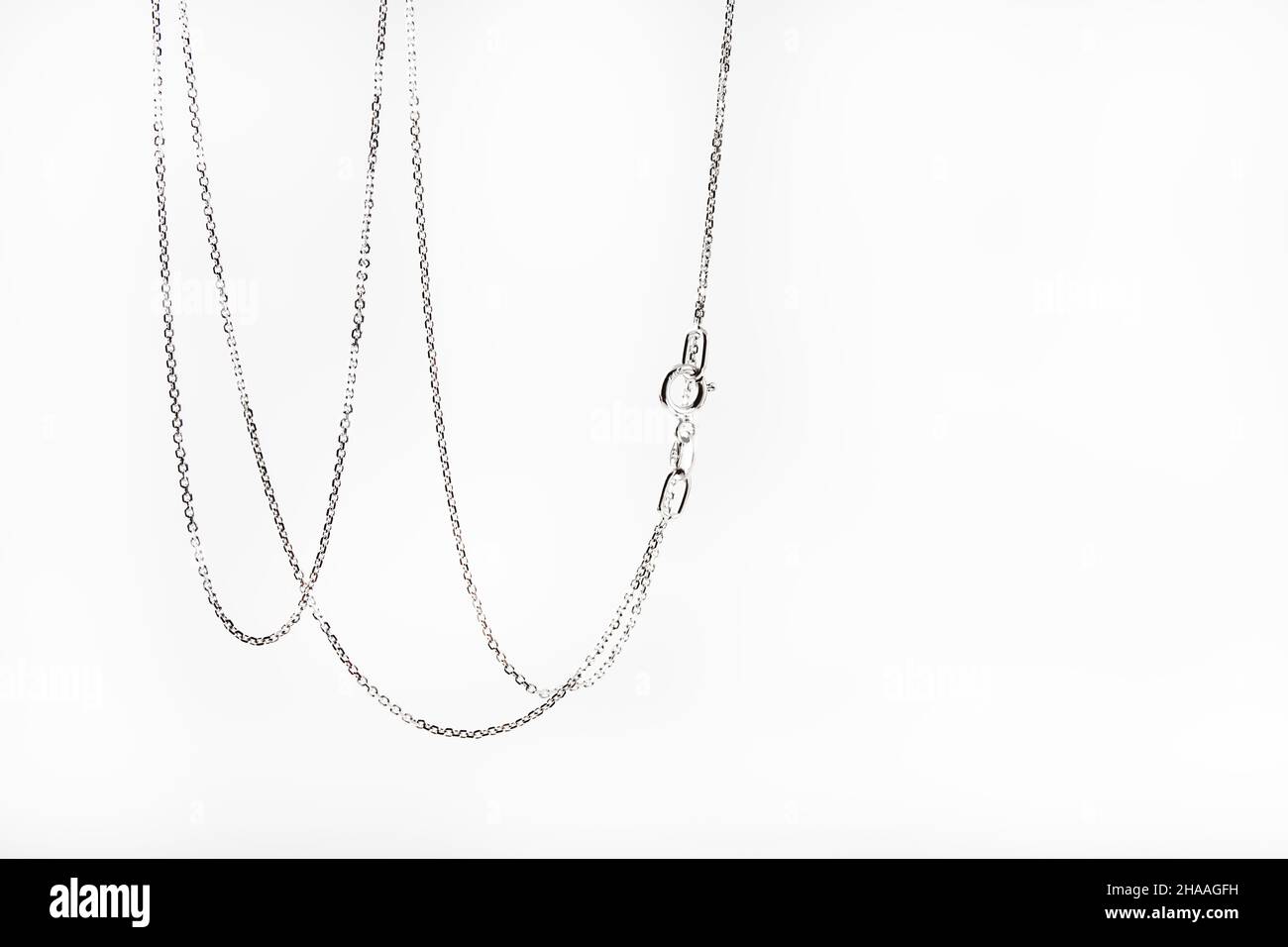 Silver chain hanging on a white background Stock Photo - Alamy