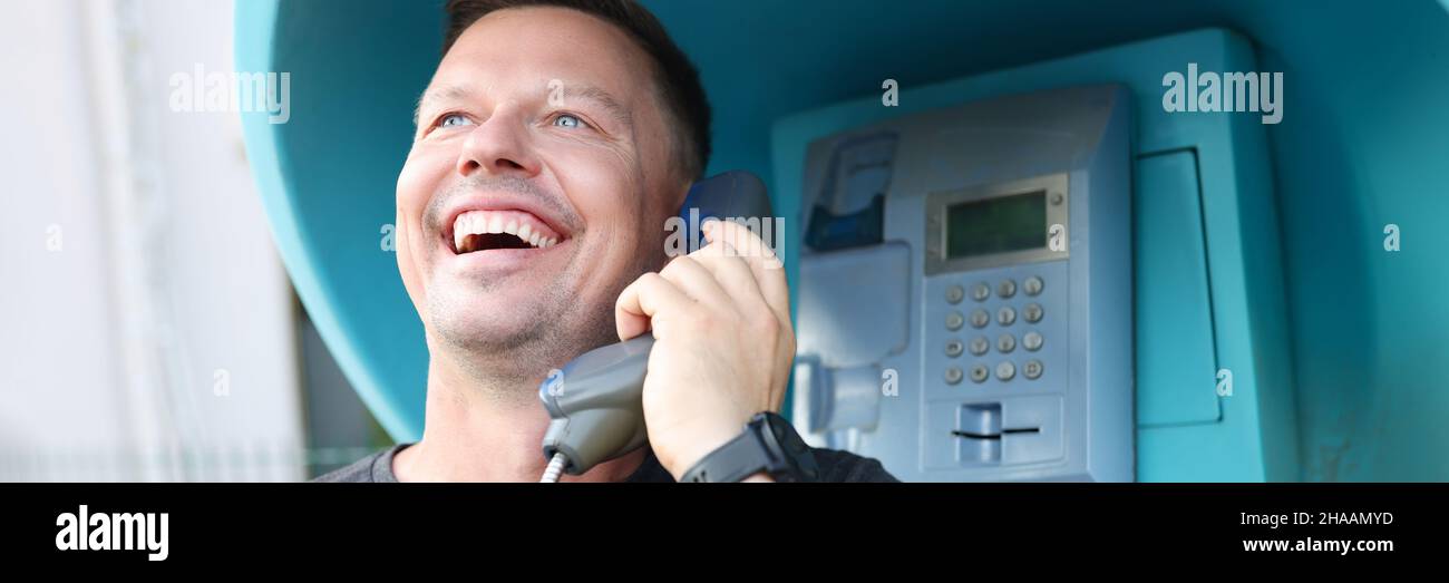 Smiling young man talking on phone booth on street Stock Photo - Alamy