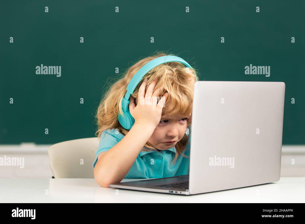 Angry sad boy wearing headphones, study with laptop in classroom ...