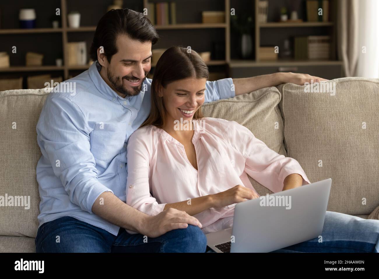 Happy cheerful millennial couple watching video, movie on laptop ...