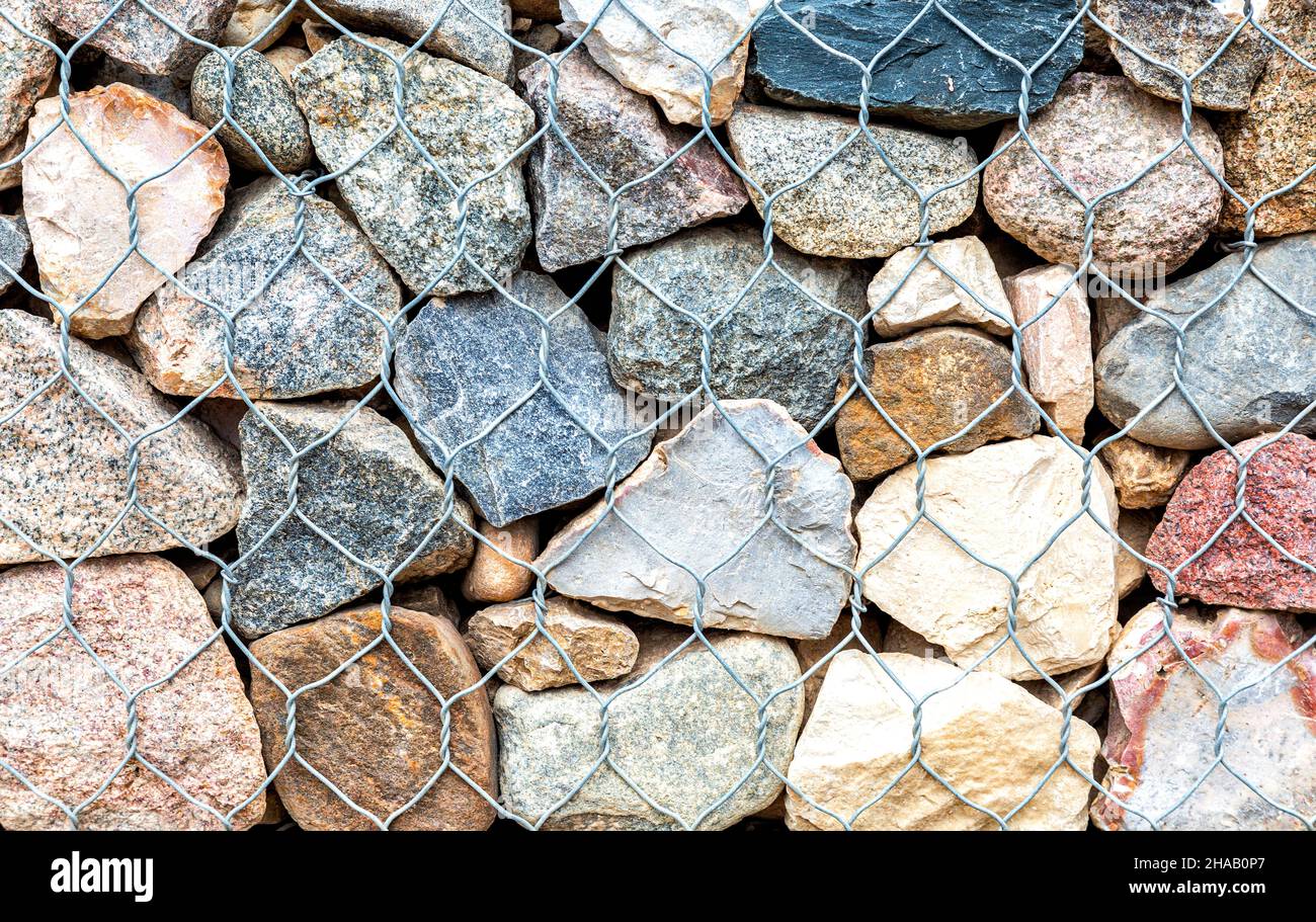 Stone wall with metal grid and rough stones as background. Rock texture ...