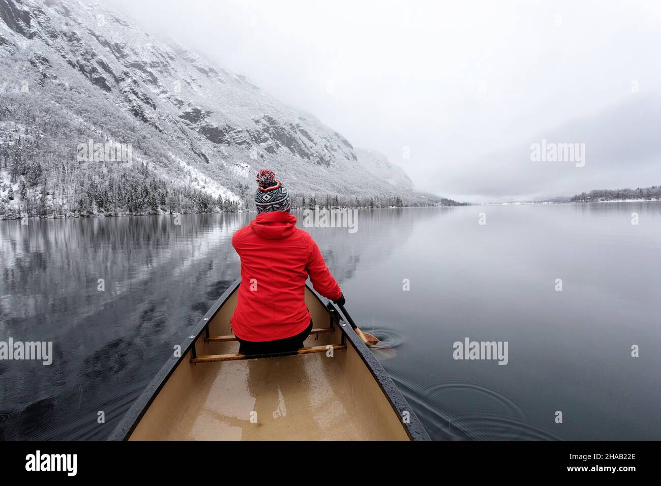 Rear view of woman paddling in red canoe on lake Bohinj in winter ...