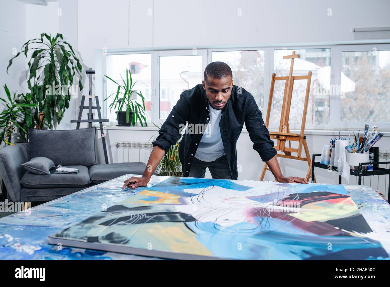 Observant black man standing next to a big canvas with painting on a ...