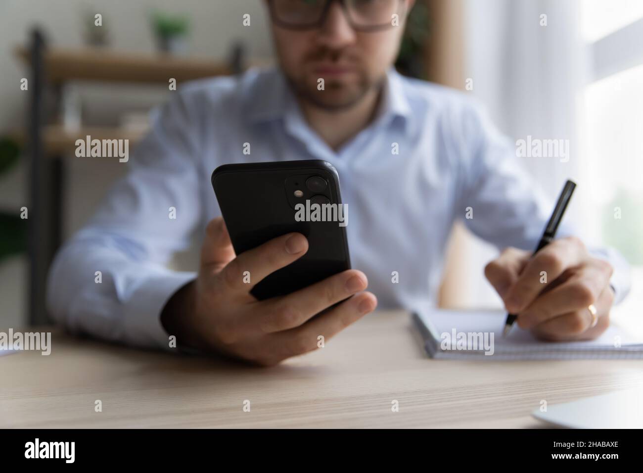 Man sit at desk holds pen, smartphone writing in notepad Stock Photo ...