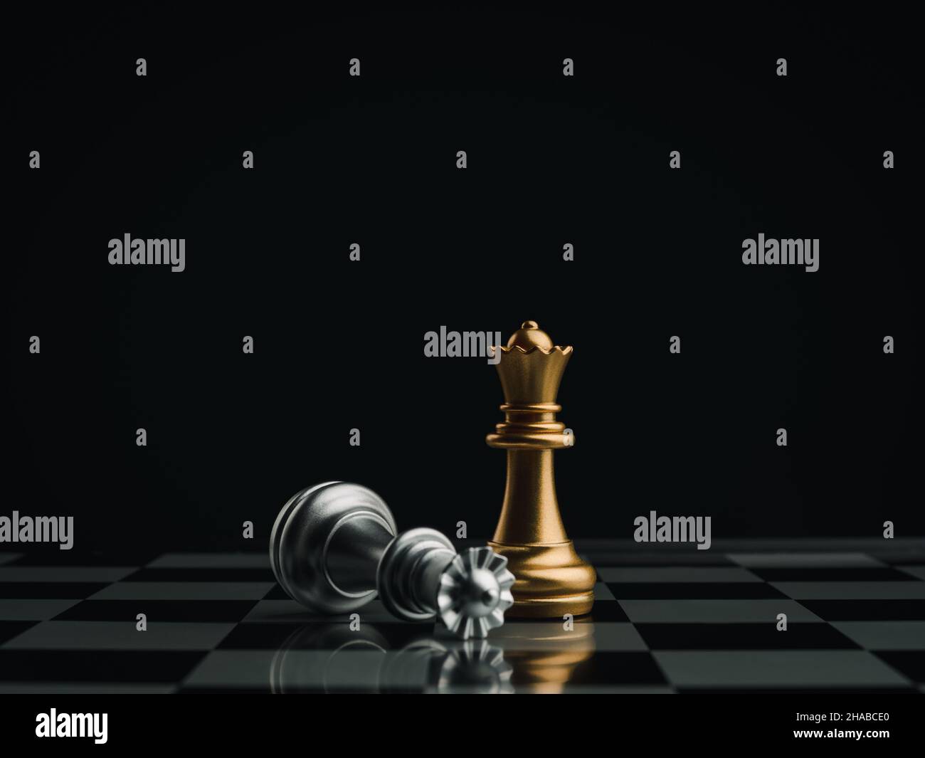 A golden queen chess piece standing with the win near a fallen silver ...