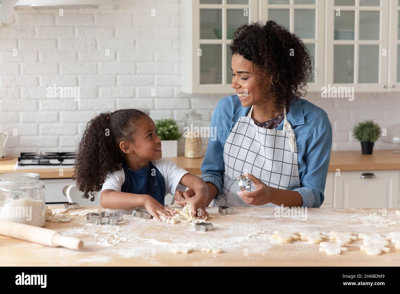 Beautiful African mother and her daughter cooking biscuits in kitchen ...