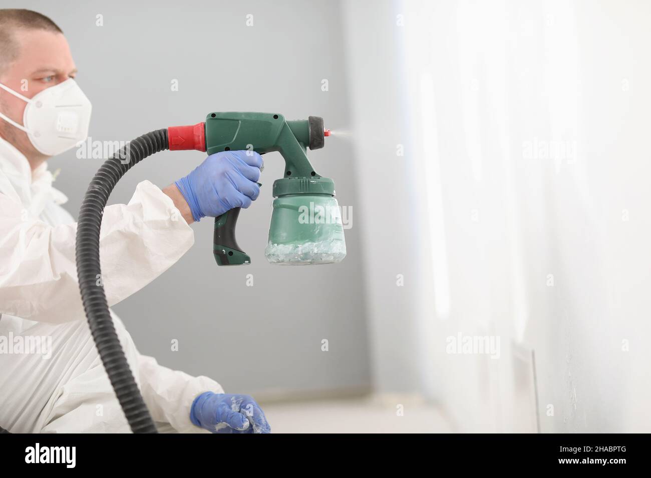 Worker using spray gun for coloring wall in white. Effective and fast ...