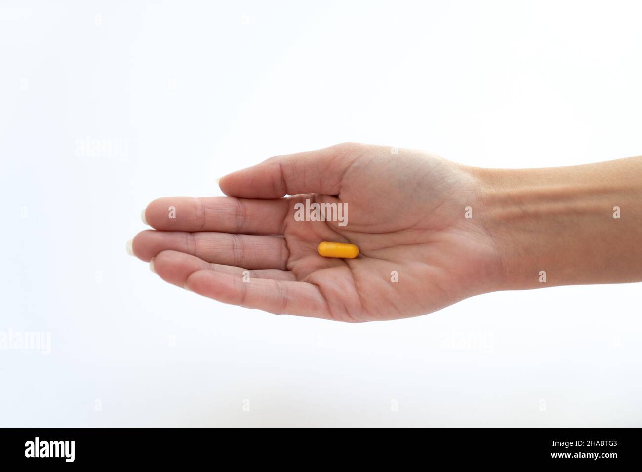 A hand holding a yellow pill on a white background Stock Photo - Alamy