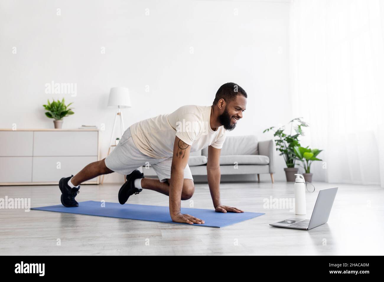 Happy young black male with beard in white sportswear do leg exercise ...