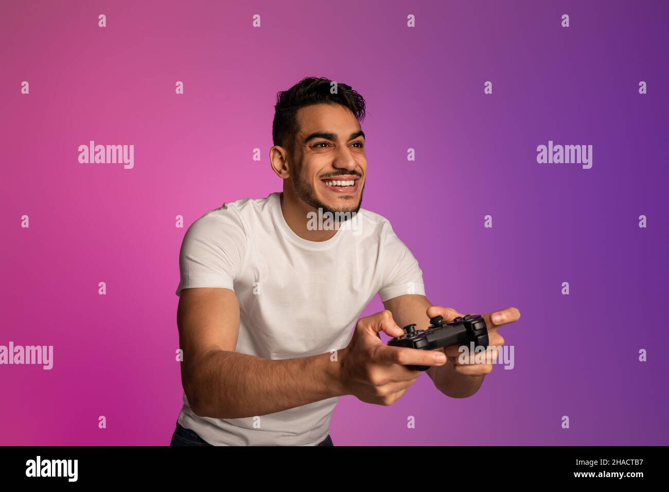 Happy young Arab guy with joystick playing video game in neon light ...
