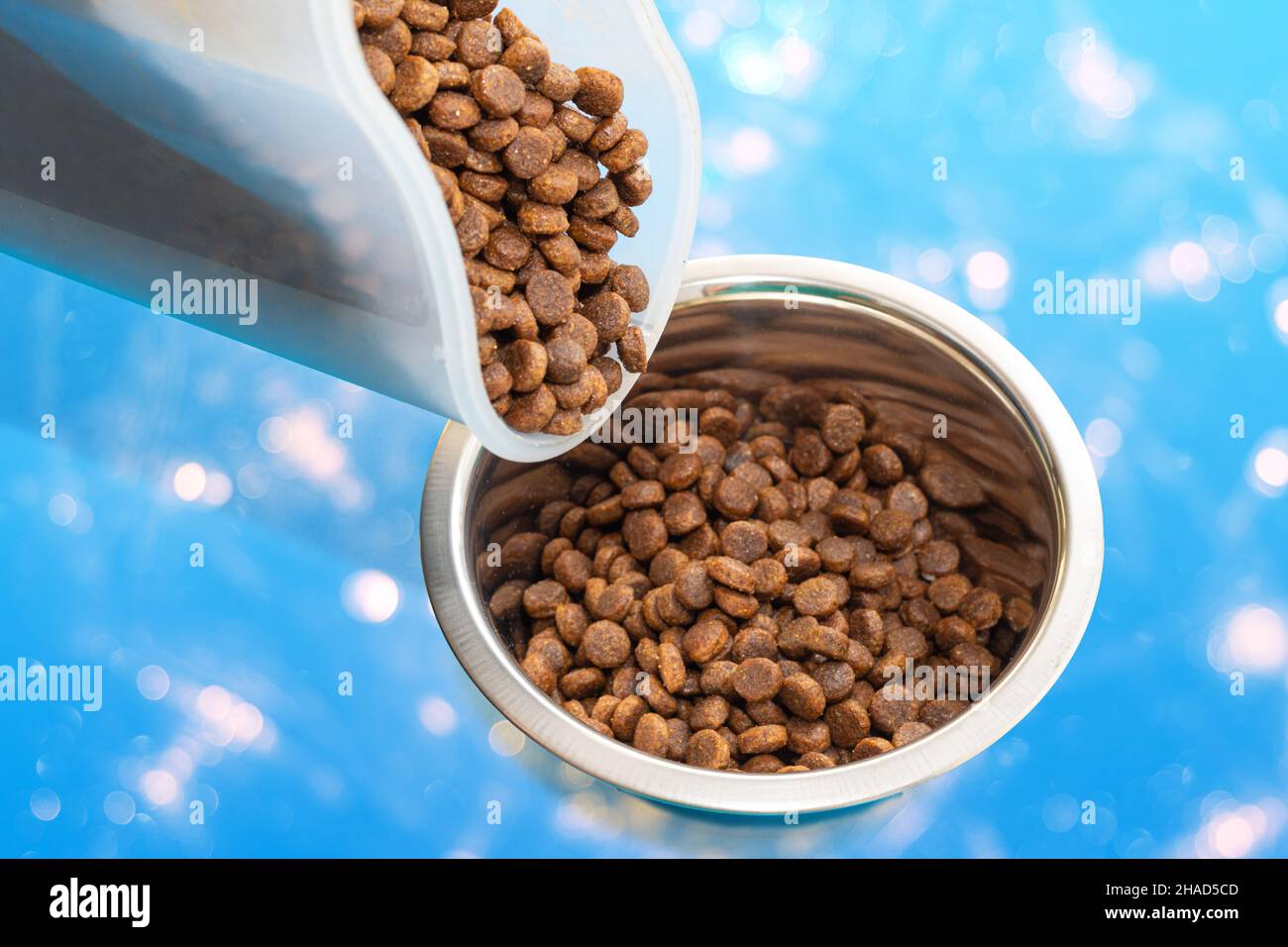A hand holds a container and puts dry animal food in a round metal bowl ...