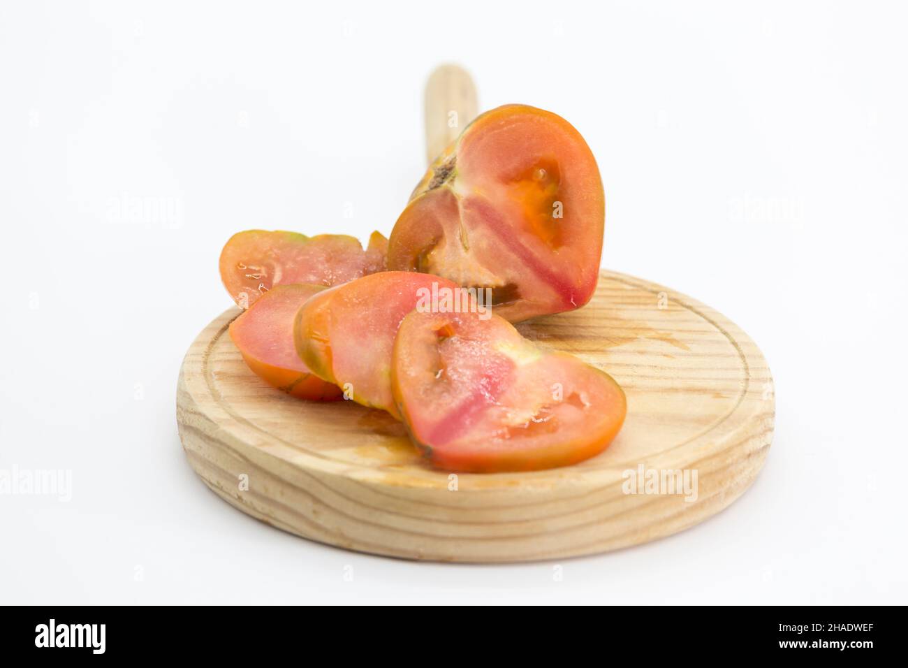 still life with a split tomato on round wooden board, placed on white ...