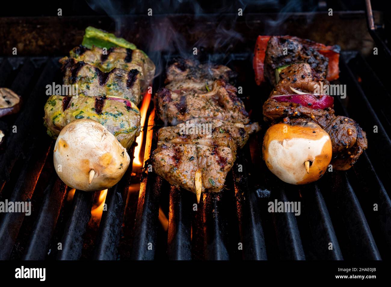 dinner being grilled in summer on a barbecue grill with flames below ...