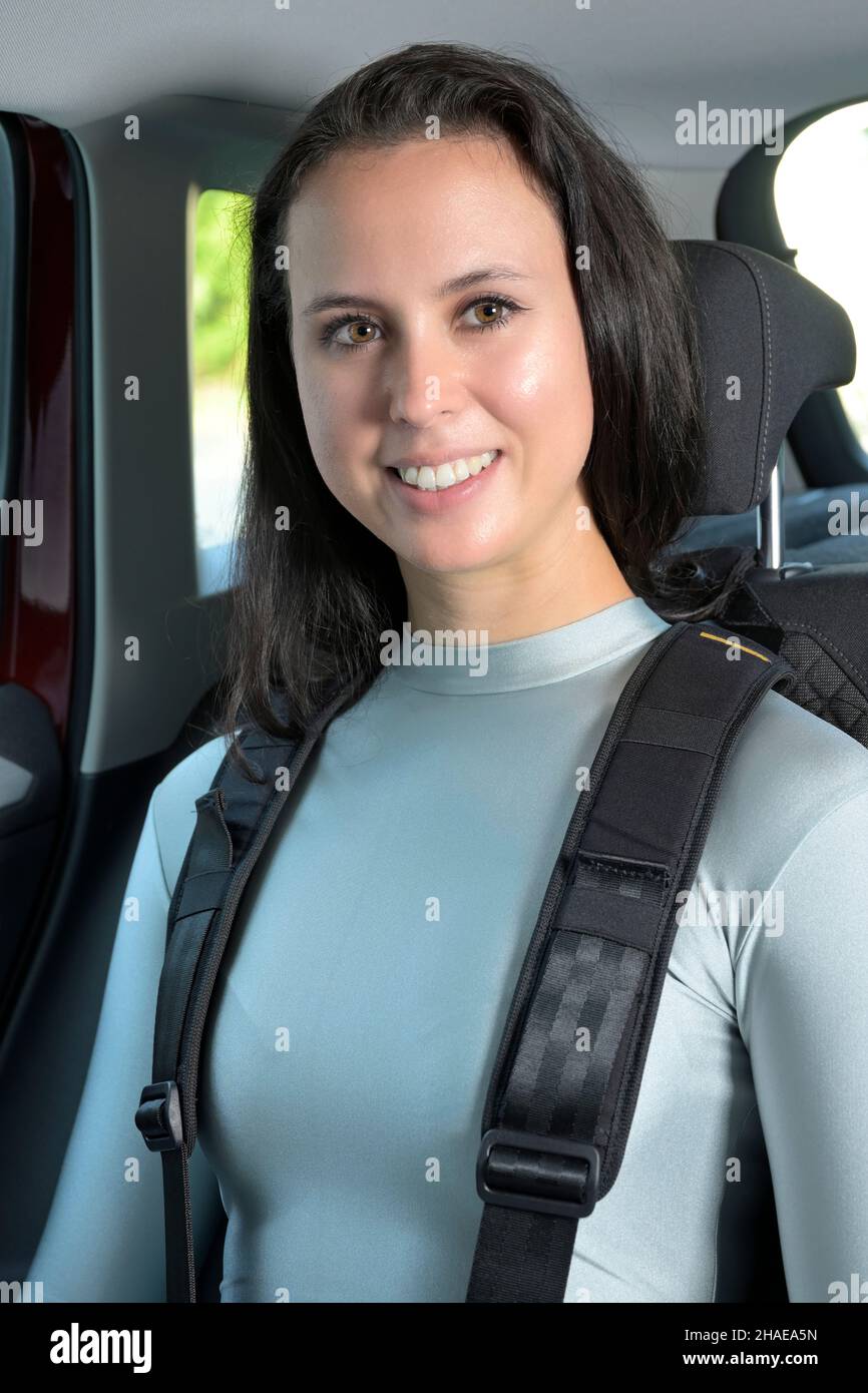 Young woman wearing a catsuit sitting in a car buckled up in a harness ...