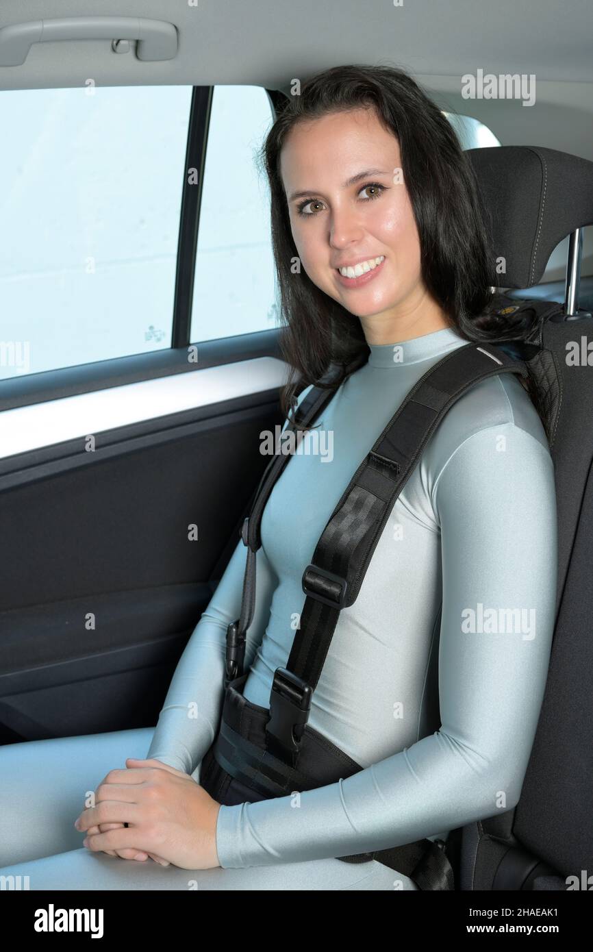 Young woman wearing a catsuit sitting in a car buckled up in a harness ...