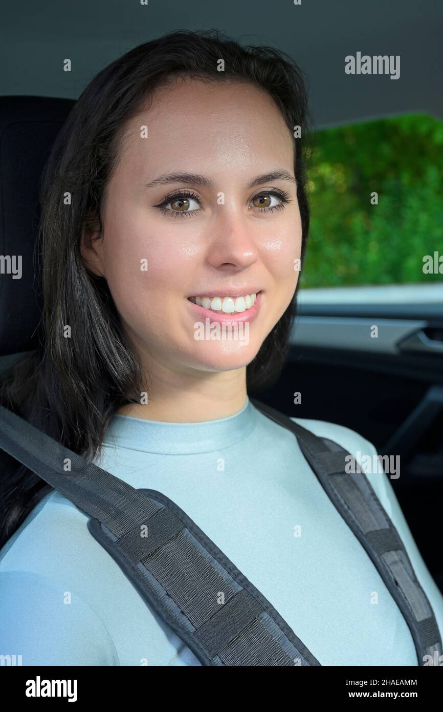 Young woman wearing a catsuit sitting in a car buckled up in a harness ...