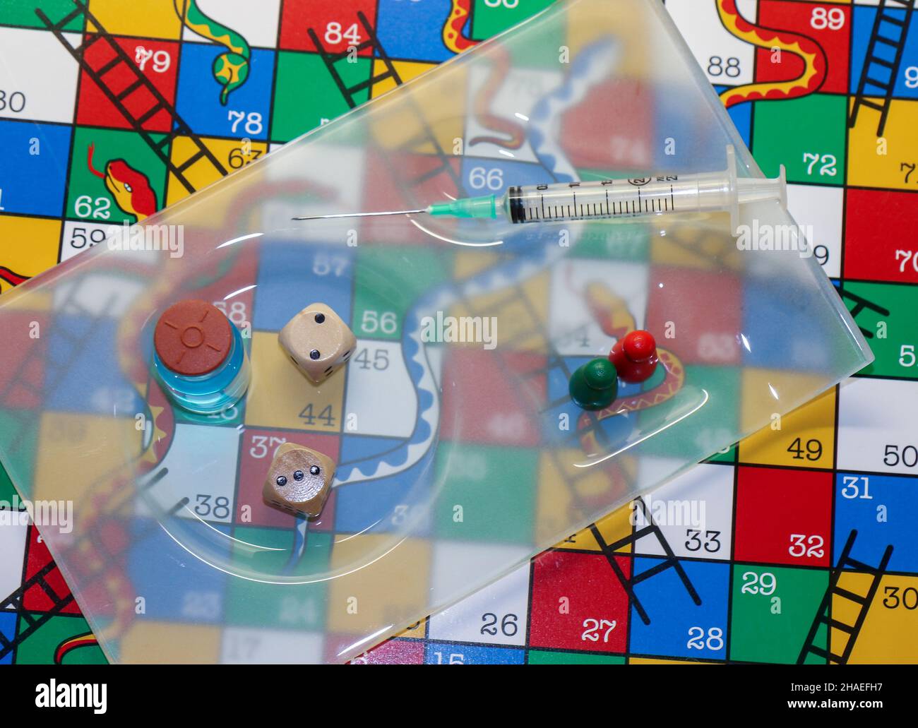 Medical syringe and vaccine vial on top of snakes and ladders board ...