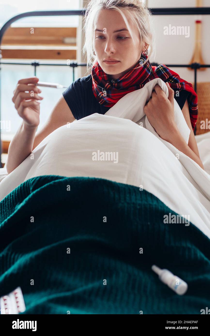 Young woman takes her body temperature and looks at the thermometer ...