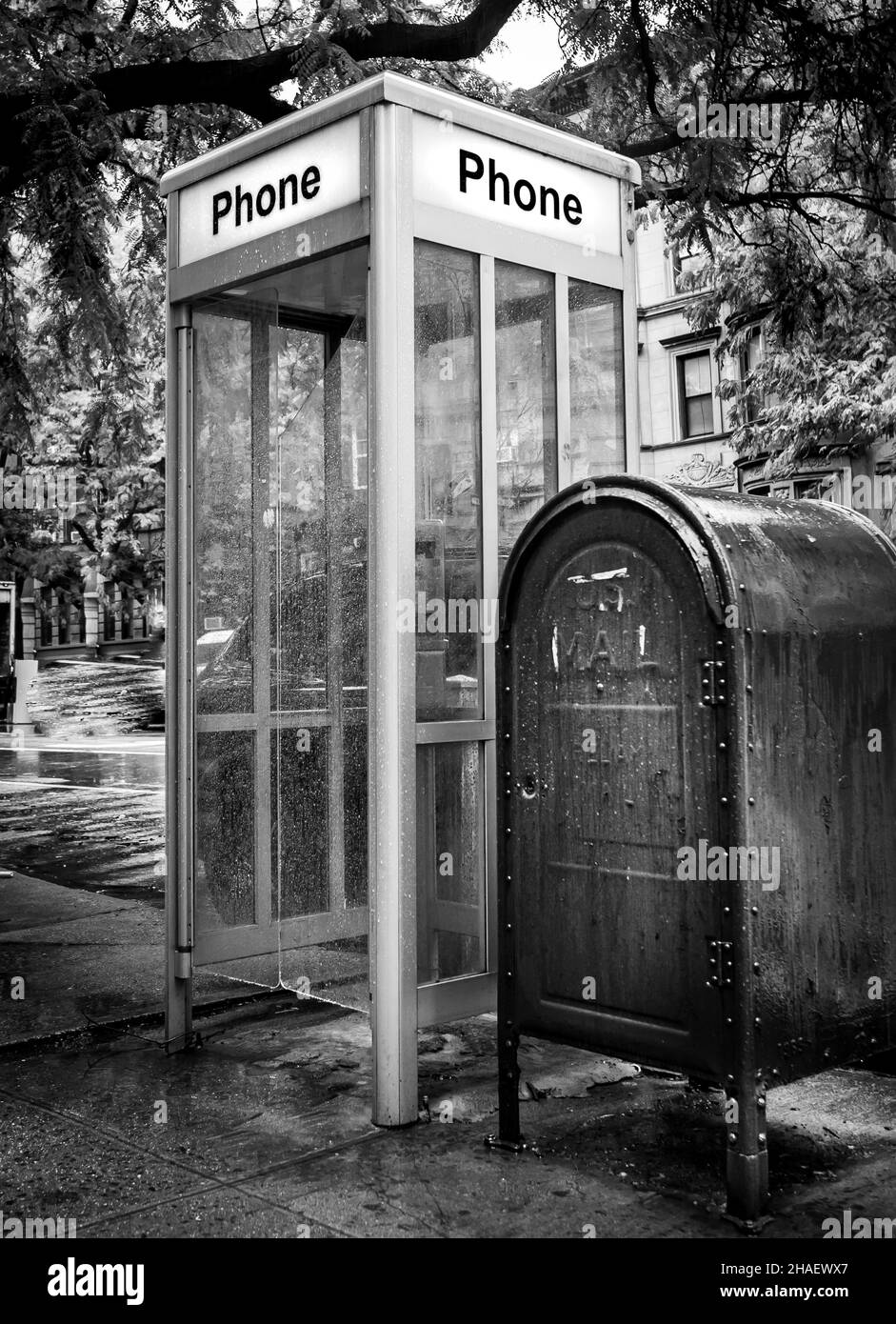 A vertical black and white shot of a phone booth and a mail box on the ...