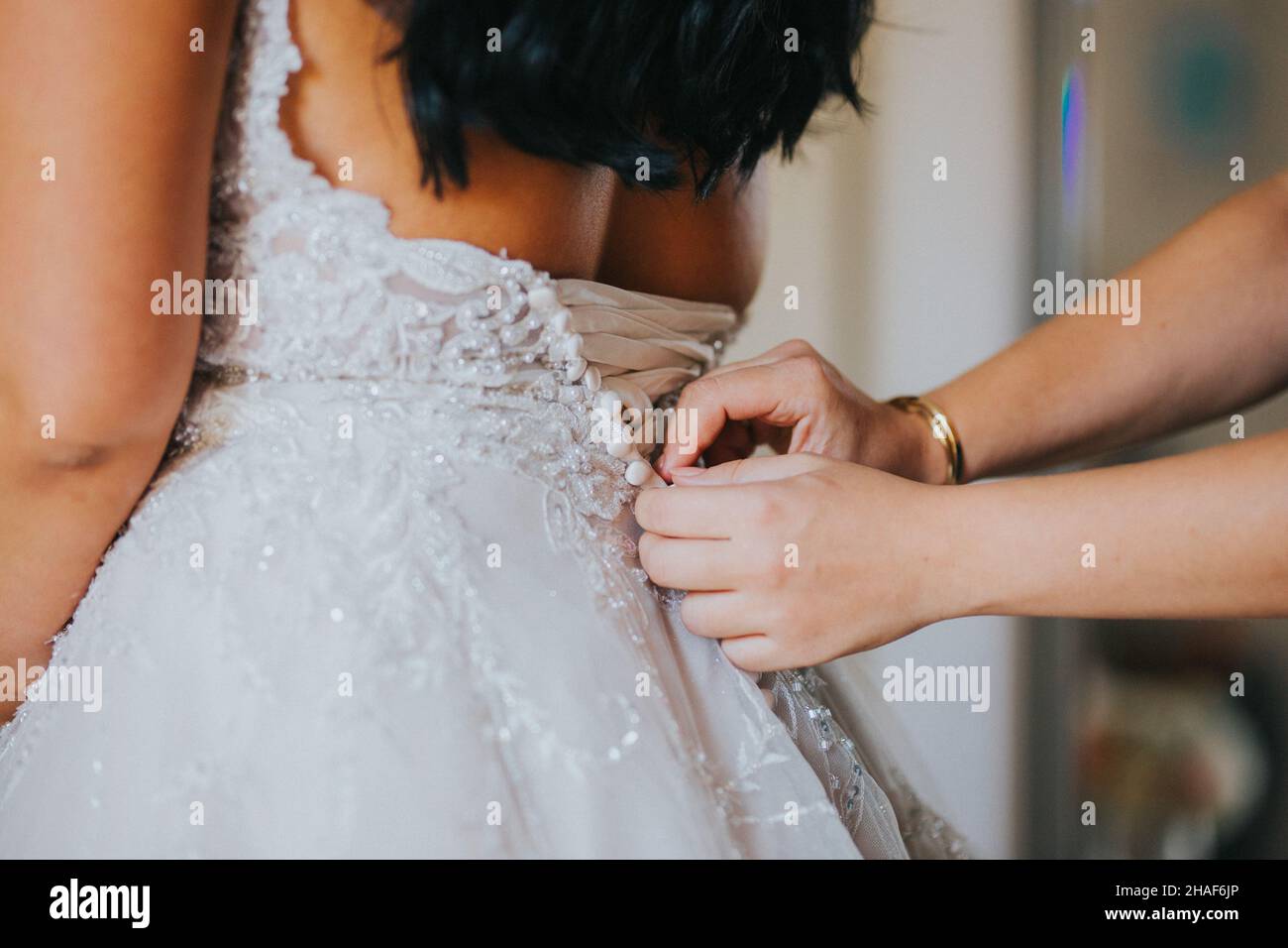 The bride putting on her dress with the help of another person and ...