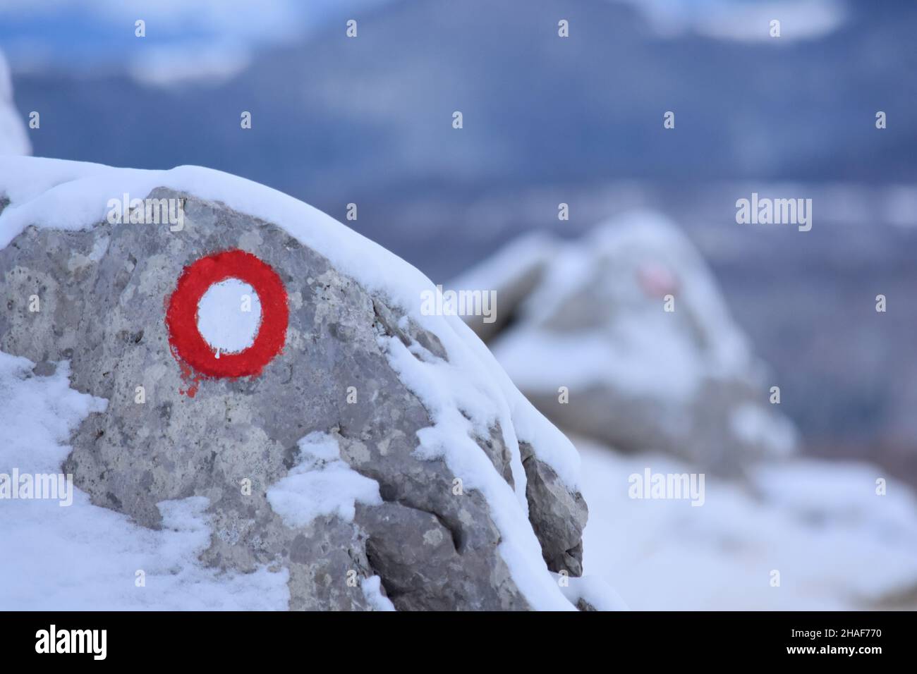 A red round with a white dot symbol on a rock fully covered in snow ...