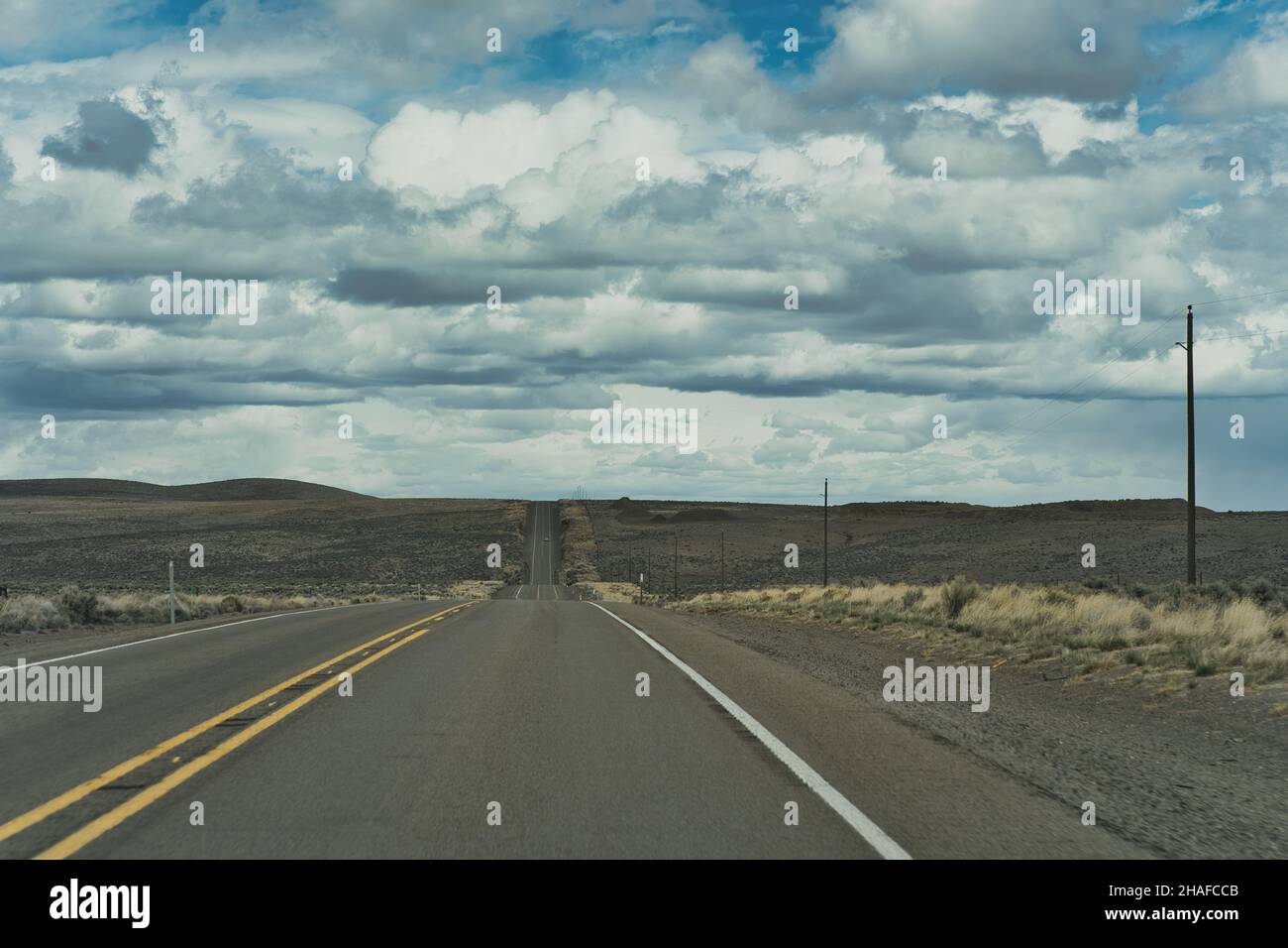 The empty U.S. 95 asphalt highway in Nevada under a blue sky with large ...