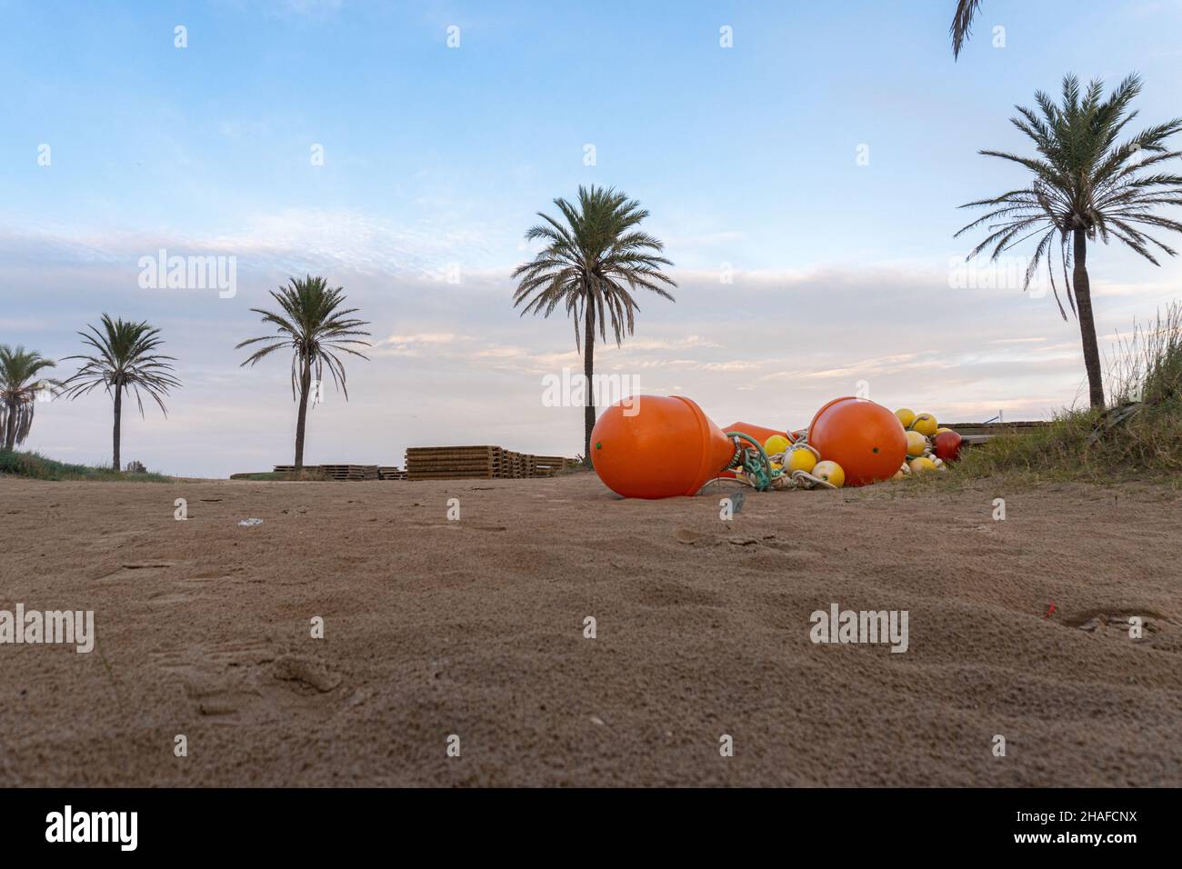 A shot of buoys of different sizes and colors thrown in the sand on a ...