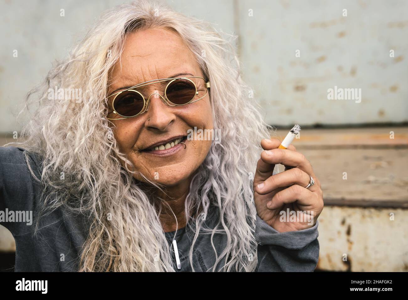 Beautiful woman with long bright curly hair is smoking a cigarette ...