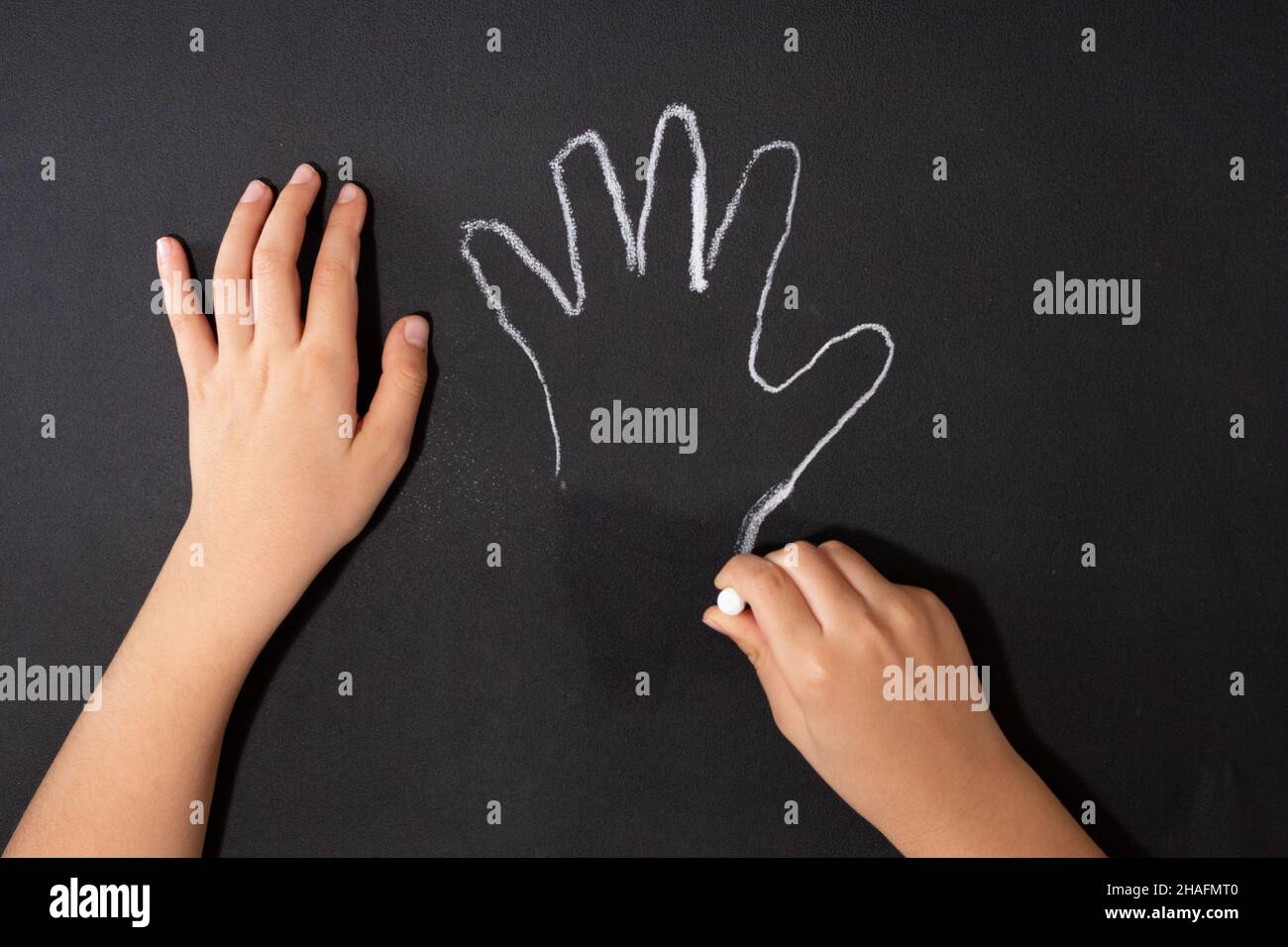 a child traces a hand with chalk on a black surface, DIY Halloween ...