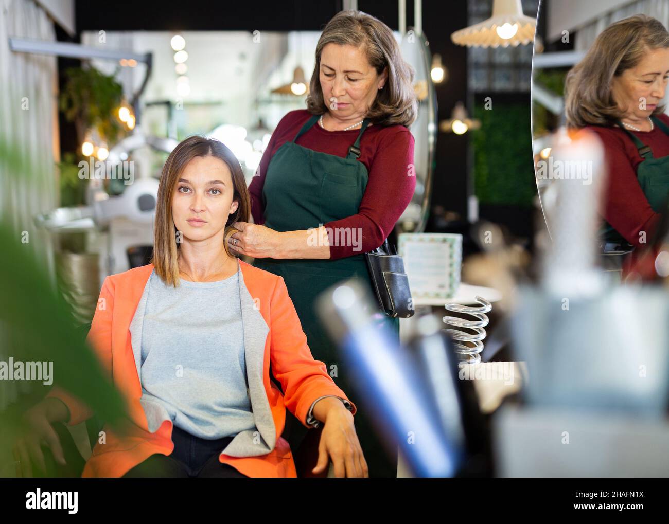Skilled aged female hairdresser offering modern hairstyling to young ...