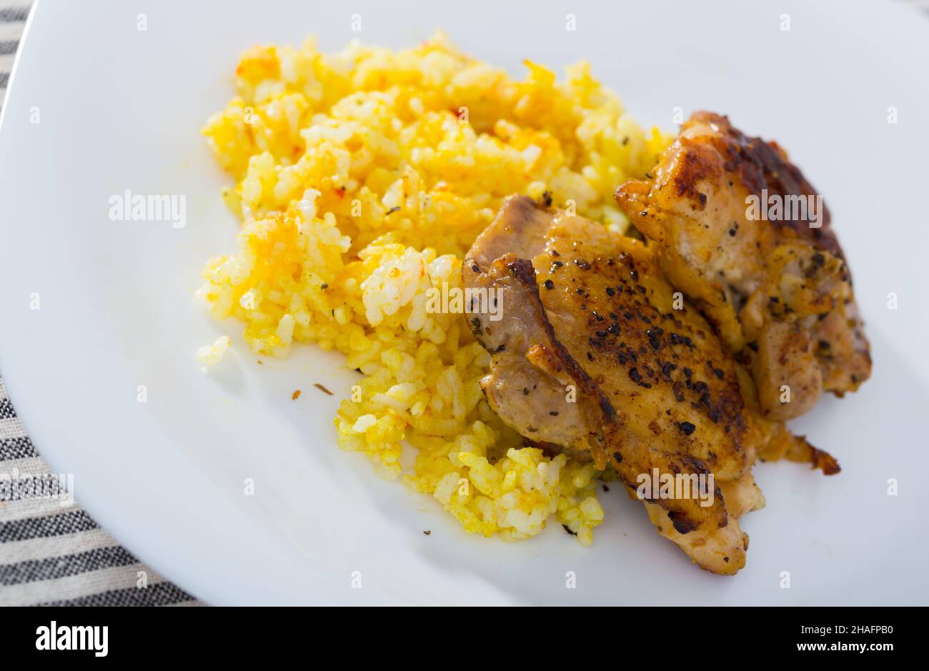 Juicy fried chicken thighs on white plate with garnish of spicy rice ...