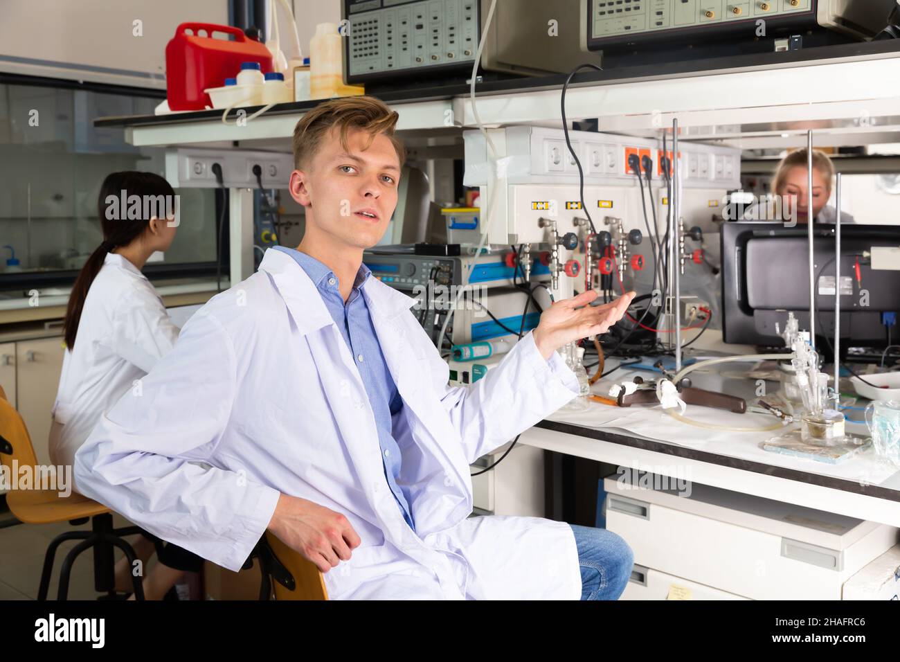 Young male scientist sitting near laboratory equipment at biochemical ...