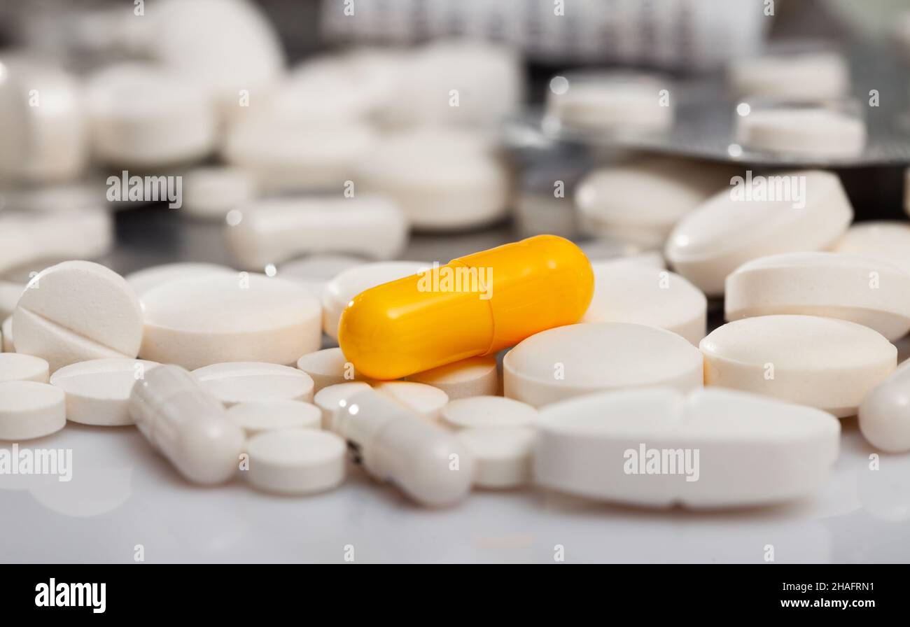 Yellow drug capsule lying among white tablets. Conceptual image of ...