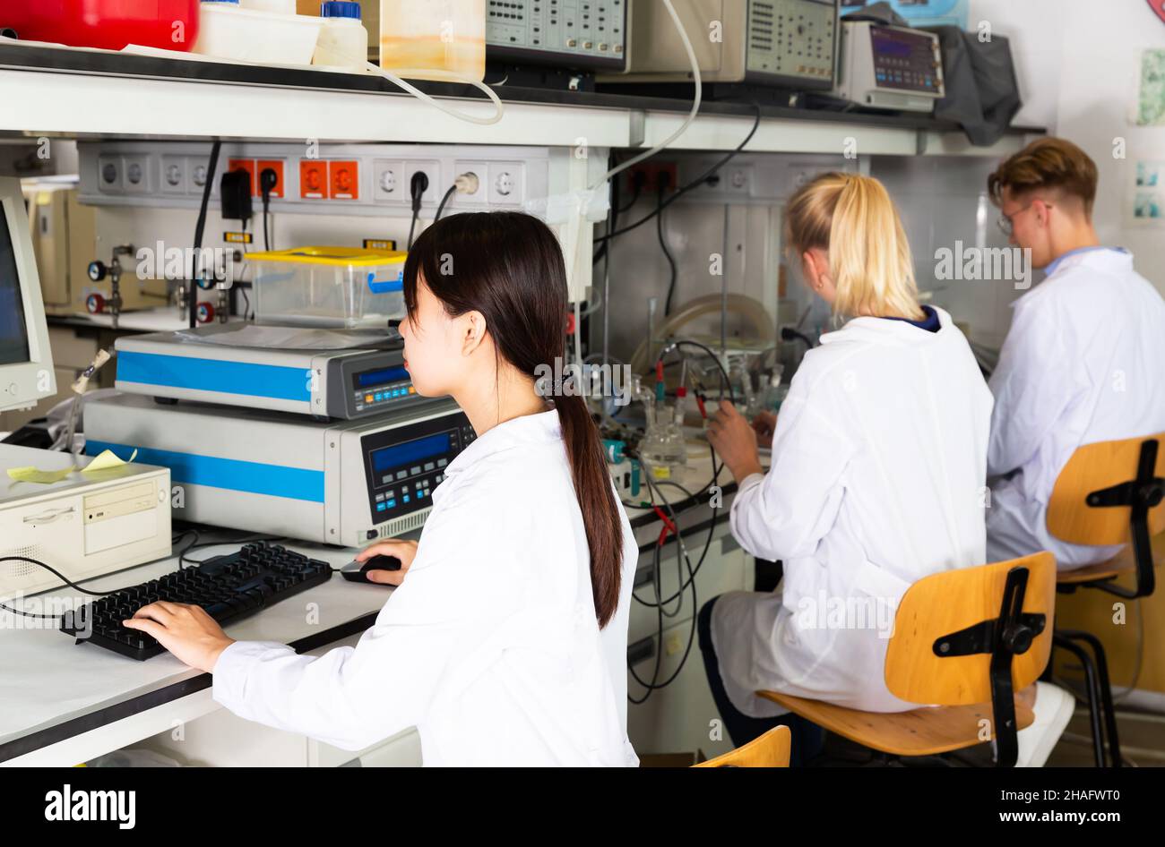 Multiracial team of students performing experiments on lab equipment in ...