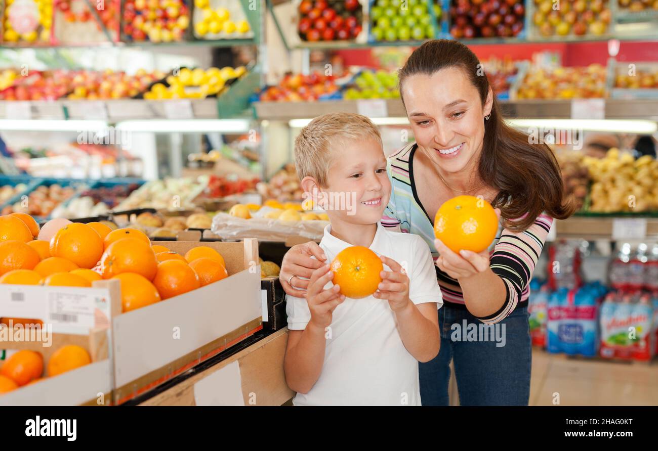 .Little child with female choosing fresh oranges at fruit department of ...